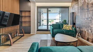 Uma sala de estar moderna com uma televisão de tela plana grande, sofás verdes, uma mesa de centro e um mural com vista para a cidade.