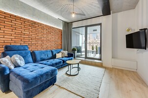 Uma sala de estar moderna com um sofá azul, uma mesa redonda pequena e uma TV fixada na parede.