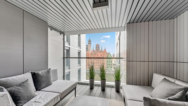 Varanda moderna com vista para um edifício histórico, sofás cinza e plantas em vasos.