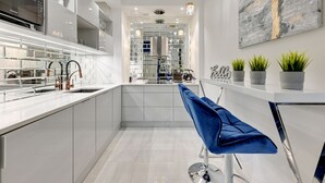 Cozinha moderna com armários brancos, eletrodomésticos de aço inoxidável e um banquinho azul.