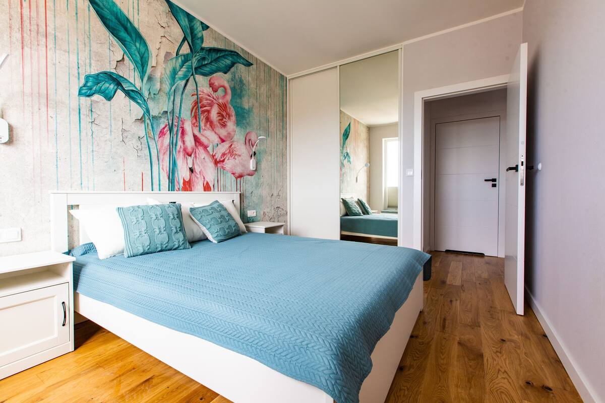 Quarto com cama, mesa de cabeceira, espelho e porta.