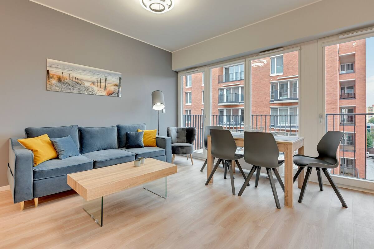 Uma sala de estar moderna com um sofá cinzento, mesa de centro de madeira e cadeiras pretas.