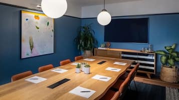 Uma sala de conferências com uma mesa de madeira comprida, seis cadeiras e uma planta grande.