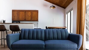 Uma sala moderna com um sofá azul, uma mesa de centro branca e uma cozinha ao fundo.