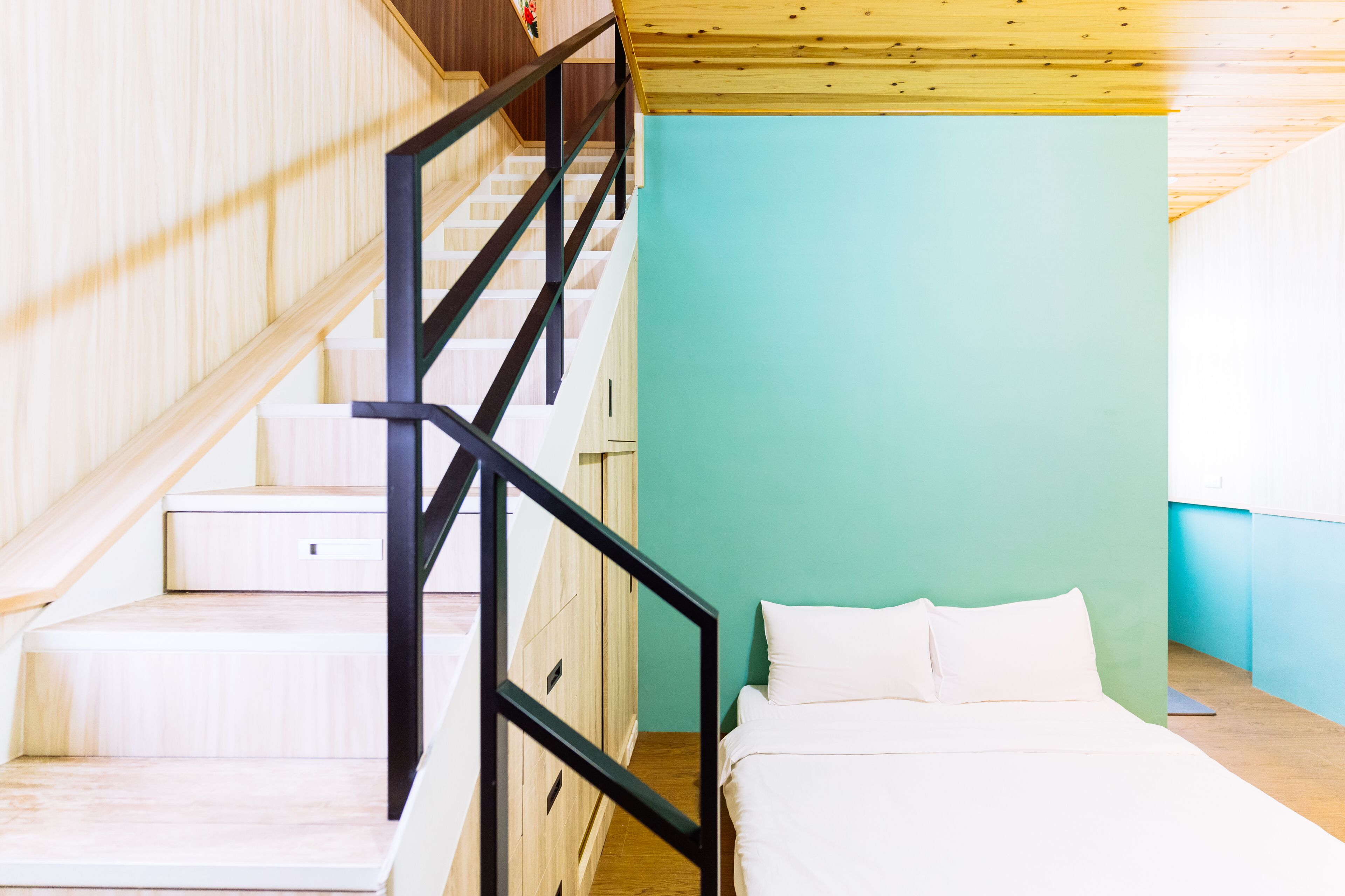 Quarto com cama, escada de madeira e parede verde-água.