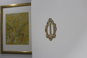 Obra de arte emoldurada de uma árvore, com moldura dourada e uma placa decorativa na parede.