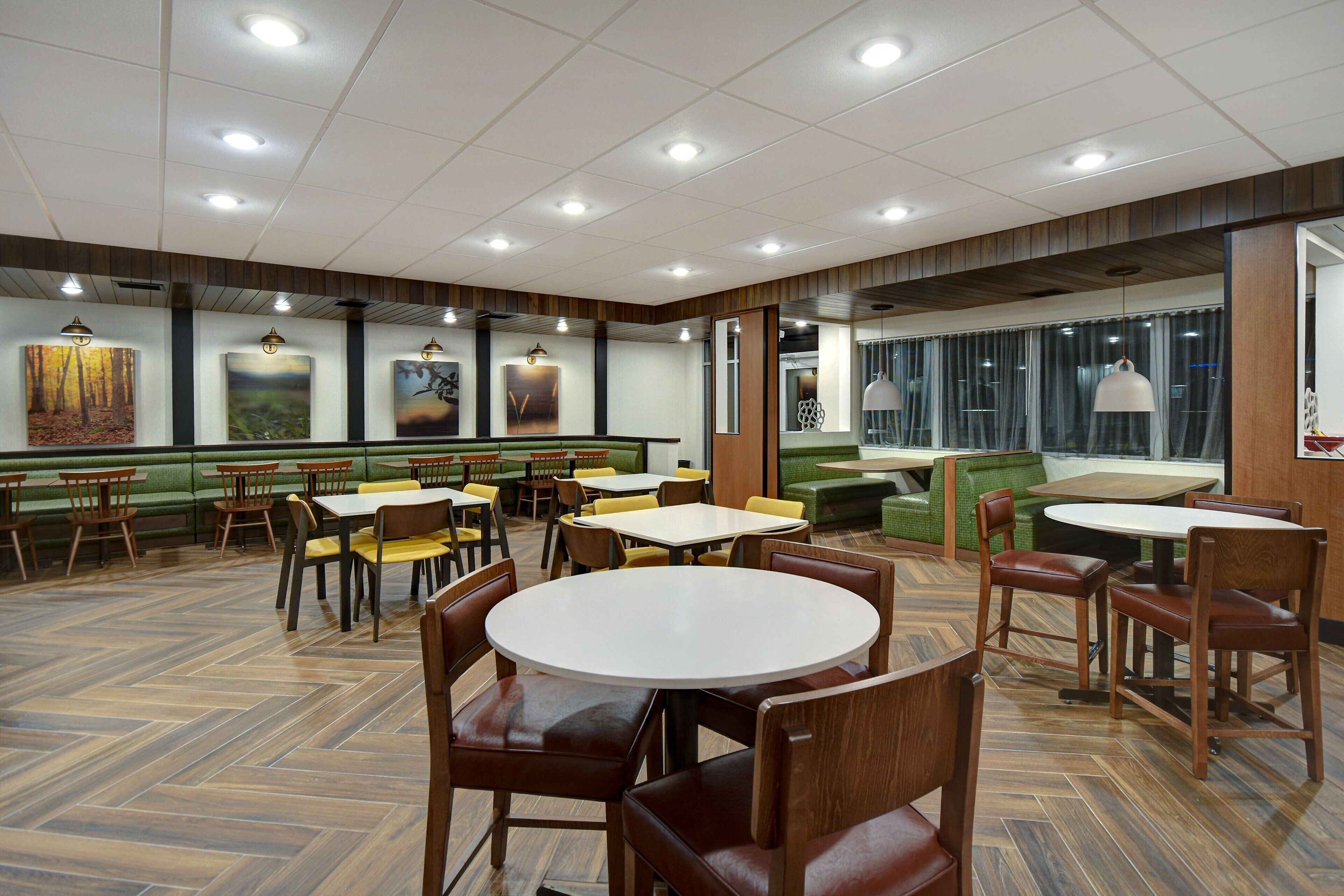 Restaurante com bancos, mesas e cadeiras, piso em padrão de herringbone e painéis de madeira nas paredes.