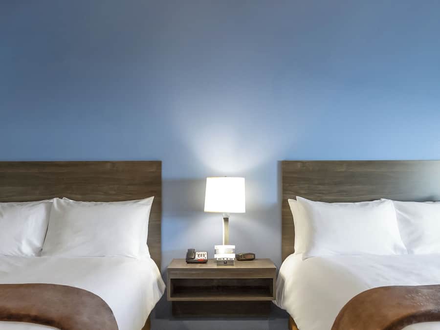 Quarto de hotel com duas camas, uma mesinha de cabeceira com abajur e um telefone.