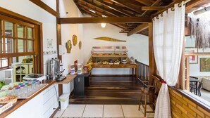 Uma cozinha com vigas de madeira, um buffet com diversos pratos e uma área de refeições com cadeiras e uma mesa.
