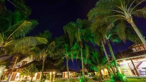 Cena noturna de um resort com palmeiras e edifícios iluminados.