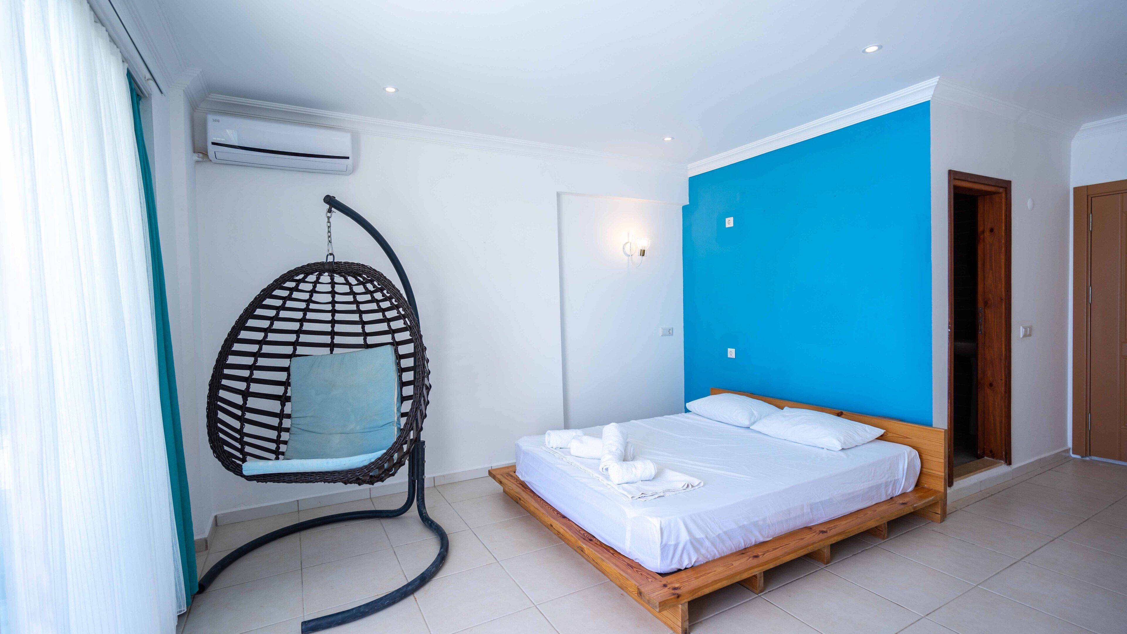 Quarto com uma cadeira suspensa, cama com roupa de cama branca e parede azul decorativa.