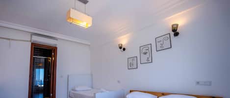 Quarto de hotel com duas camas, cabeceira de madeira, roupa de cama branca, um banco e obra de arte na parede.