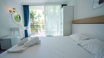 Quarto de hotel com cama, escrivaninha, cadeira e varanda com vista para árvores.