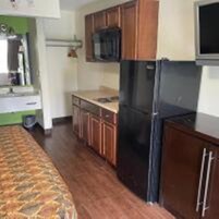 Cozinha compacta com armários de madeira, geladeira preta e micro-ondas.
