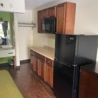 Cozinha compacta com armários de madeira, uma geladeira preta e um micro-ondas sobre a bancada.