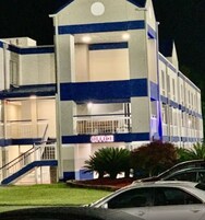 Um hotel com fachada azul e branca, um letreiro indicando “OFFICE” e uma escadaria que leva à entrada.