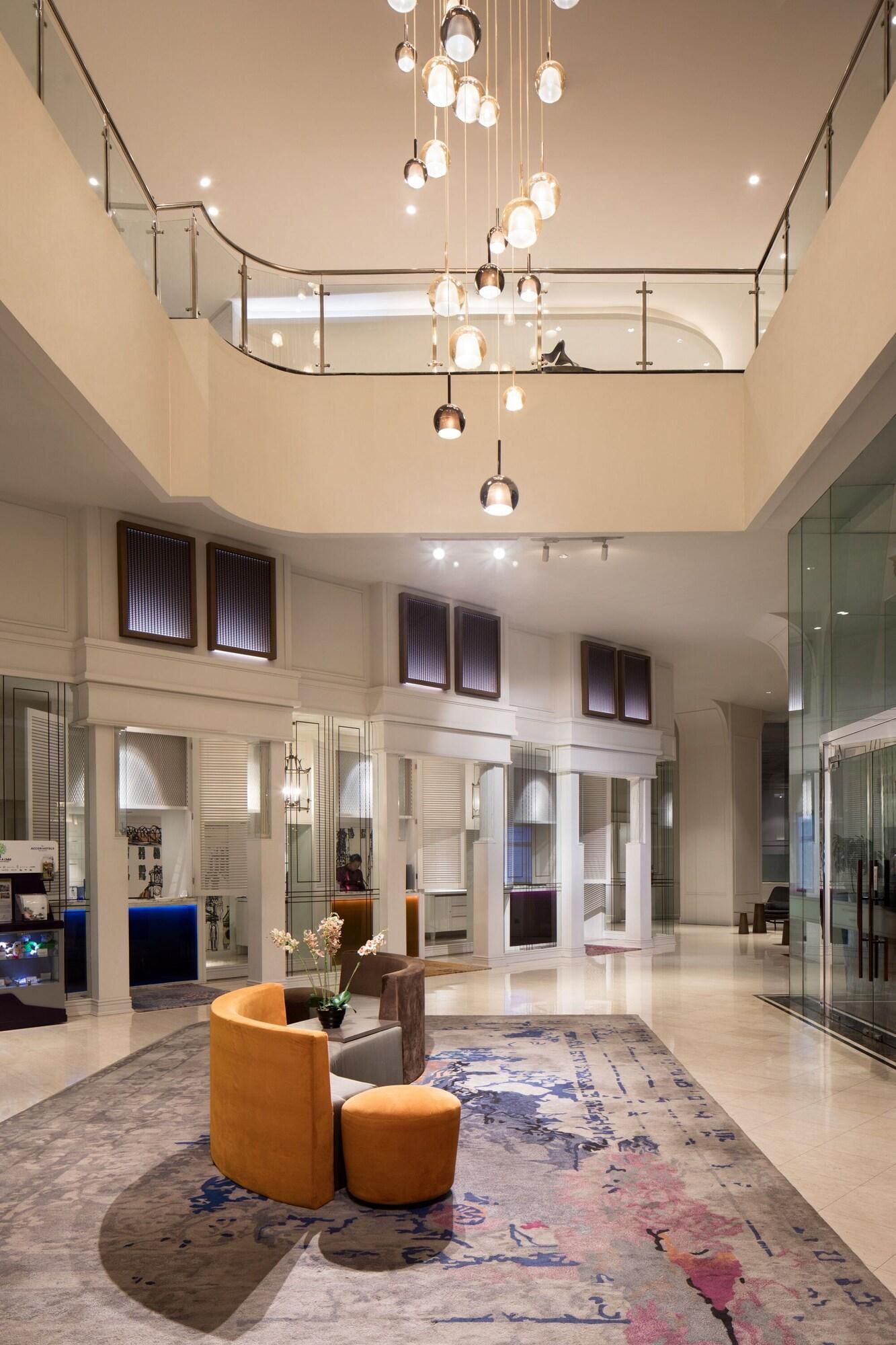 Um hall amplo com teto alto, diversas áreas de estar e um lustre central.