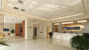 Um saguão de hotel com balcão de recepção, área de estar e uma grande planta em vaso.