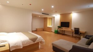 Quarto de hotel moderno com uma cama grande, um sofá, uma escrivaninha com computador e uma televisão.