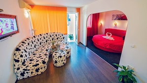 Quarto de hotel moderno com sofá curvo, cama vermelha e pequena mesa com uma abacaxi.