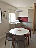 Cozinha moderna com armários brancos, painel de fundo vermelho e área de jantar com mesa e cadeiras redondas.
