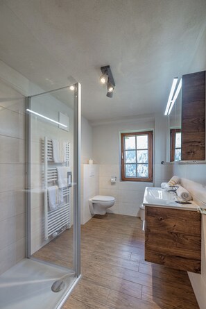 Um banheiro moderno com box de vidro, toucador de madeira e janela que proporciona luz natural.