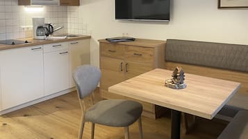 Uma cozinha compacta com micro-ondas, cafeteira e TV de tela plana. Há uma mesa de jantar com um centro de mesa decorativo e um banco.