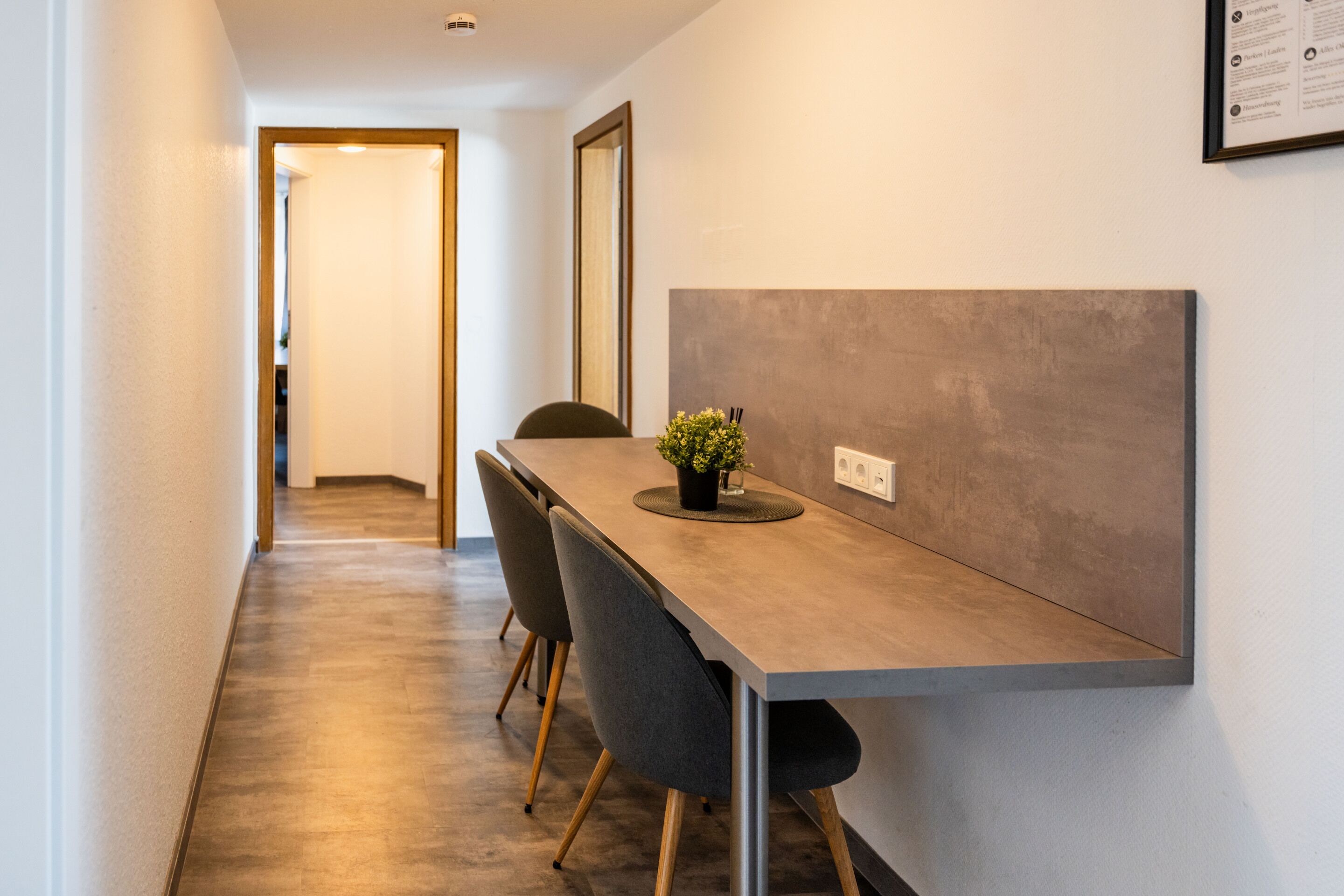 Uma área de refeições moderna com uma mesa comprida, cadeiras e um vaso com planta.