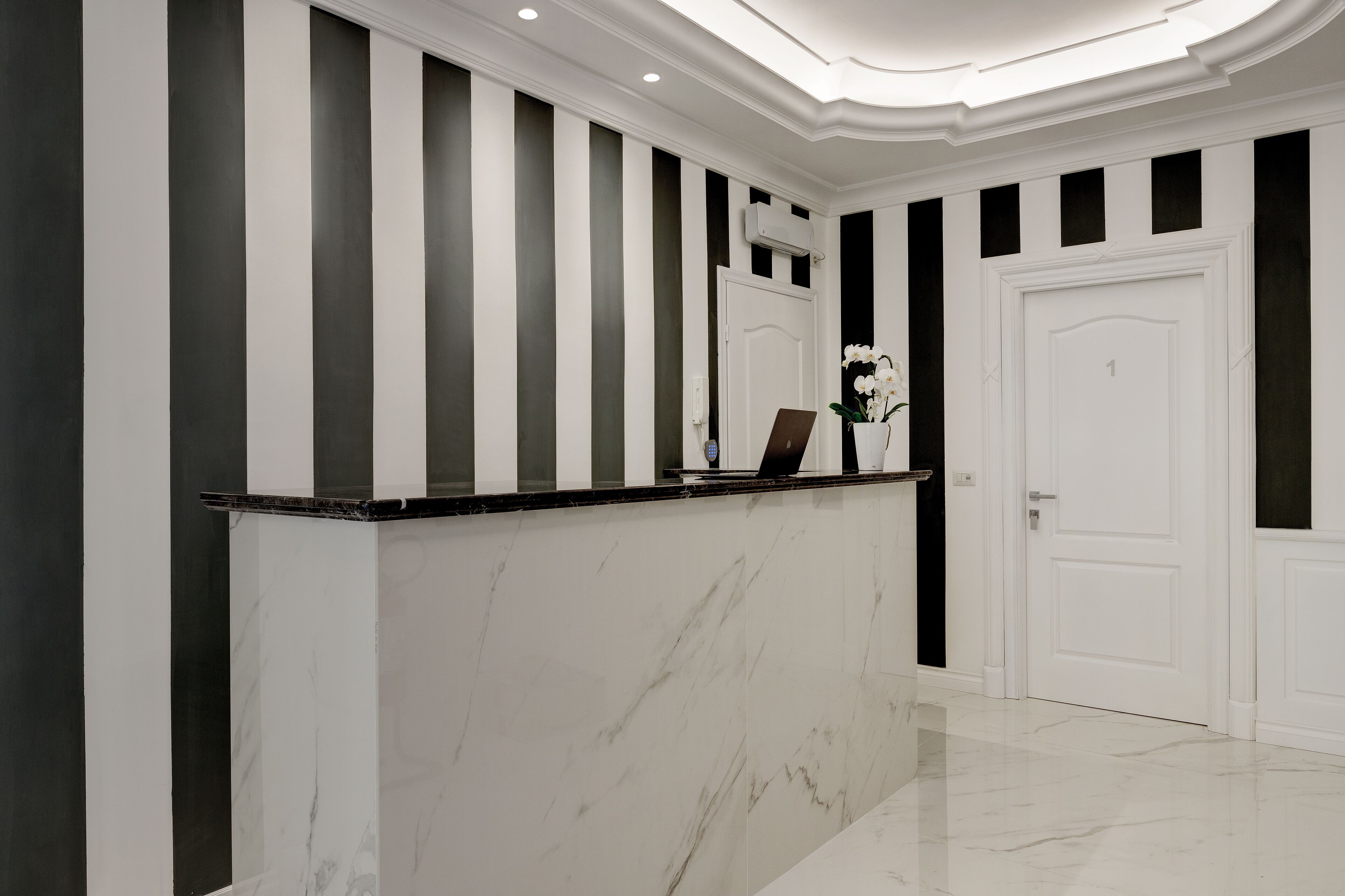 Uma área de recepção com balcão de mármore, porta branca e parede listrada em preto e branco.