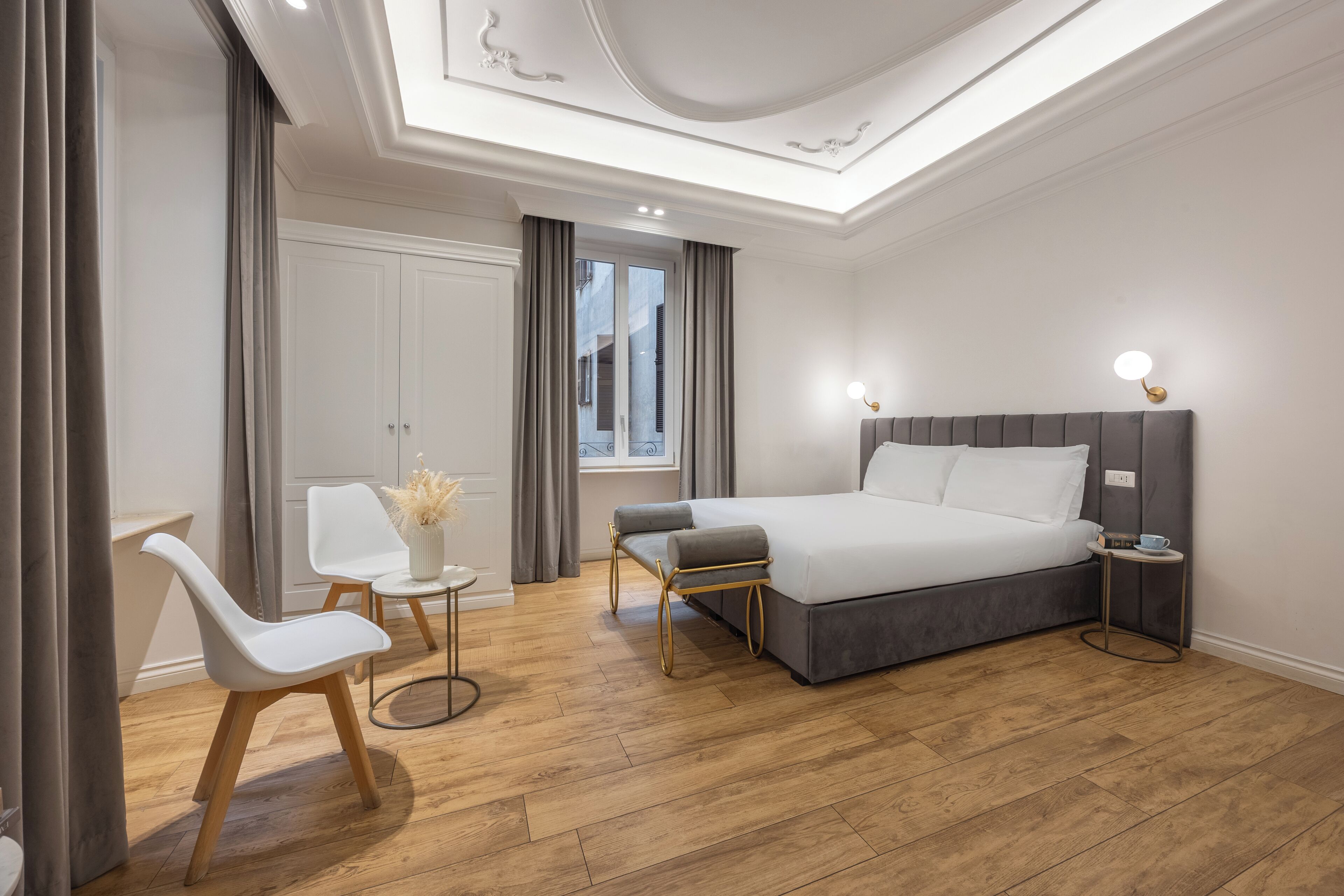 Quarto moderno com uma cama grande, mesas de cabeceira, uma cadeira e uma janela com cortinas.