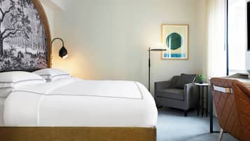 Quarto de hotel com cama, escrivaninha, cadeira, luminária de chão e um quadro na parede.