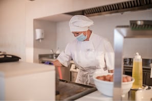 Um chef com uniforme branco preparando comida em uma cozinha moderna, com eletrodomésticos de aço inoxidável e uma disposição limpa e organizada.