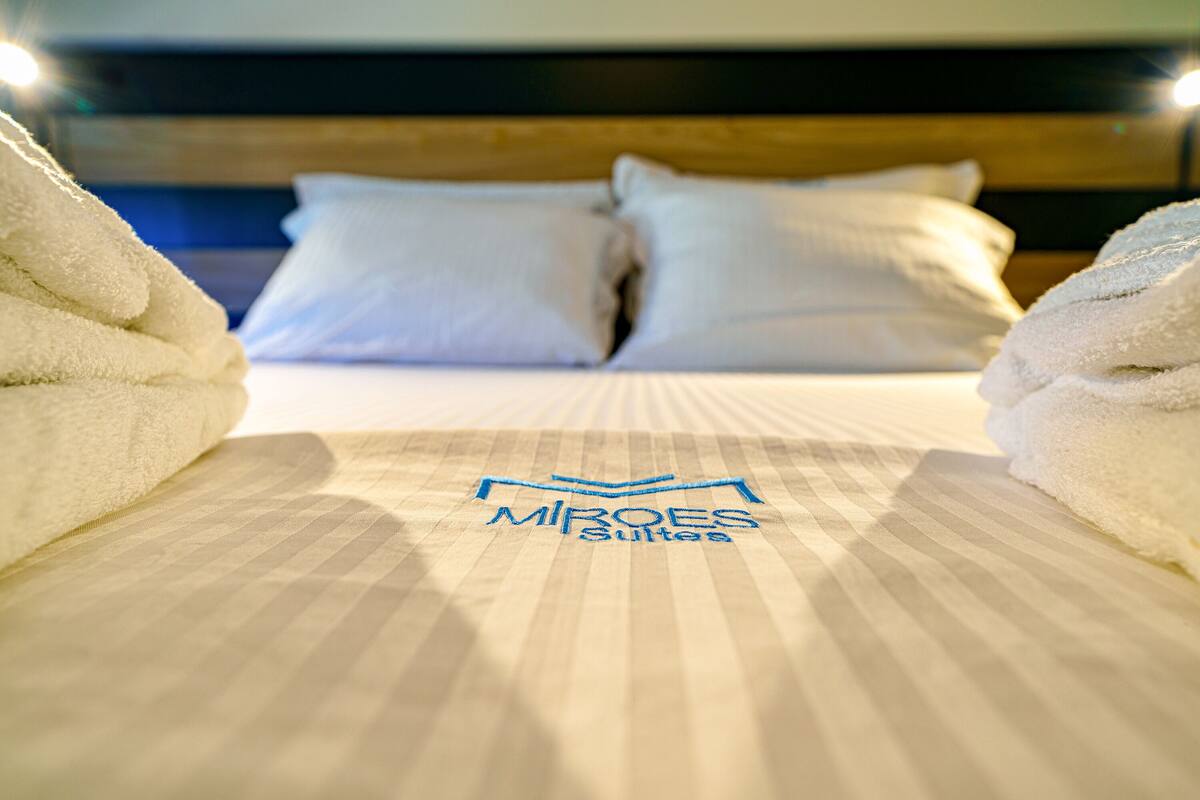 Cama de hotel com logotipo, almofadas brancas e toalhas dobradas.