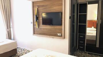Quarto de hotel com cama, televisão presa a um painel de madeira, guarda-roupa e banheiro com cortina.