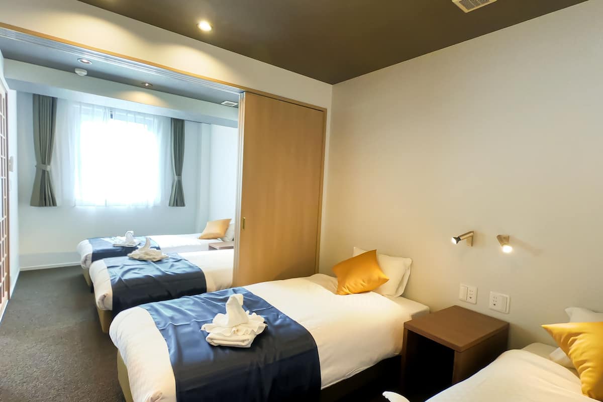 Quarto de hotel com duas camas, uma pequena mesa de cabeceira e um espelho grande.
