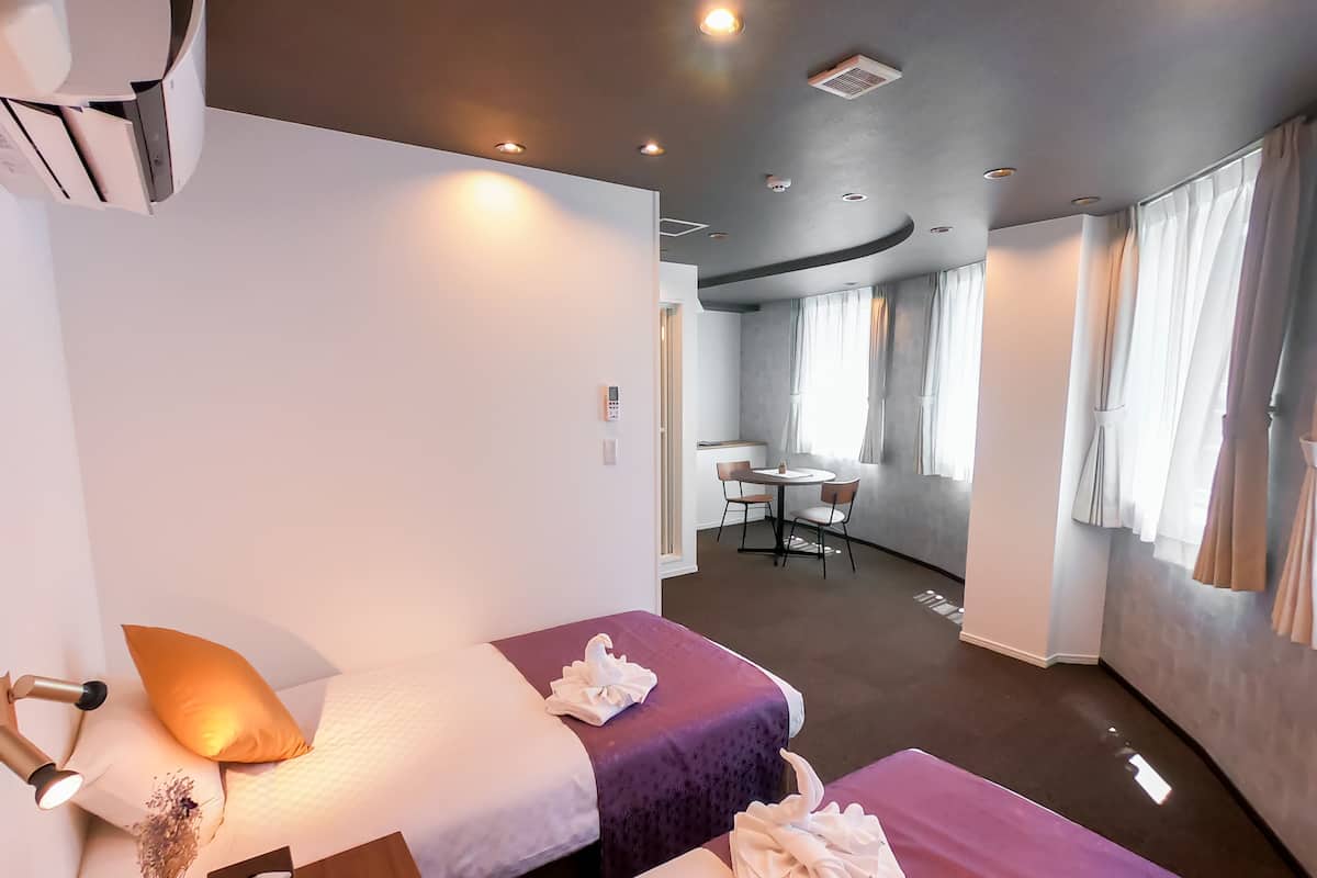 Quarto de hotel com duas camas, uma mesa pequena com cadeiras e vista para a sala de jantar.