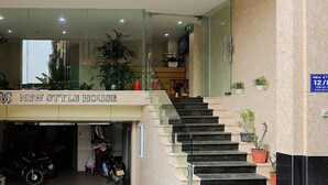 Entrada de hotel com placa indicando 'NEW STYLE HOUSE', uma escadaria que leva a um segundo andar e uma área de estacionamento abaixo.