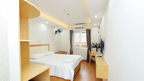 Quarto de hotel com cama, escrivaninha, cadeira, televisão e janela com cortinas.