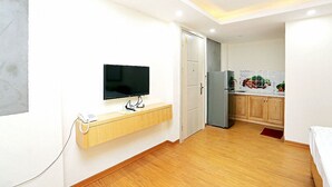 Um apartamento moderno com televisão de tela plana fixada em um console de madeira, geladeira e área de cozinha com armários de madeira e painel de azulejos.