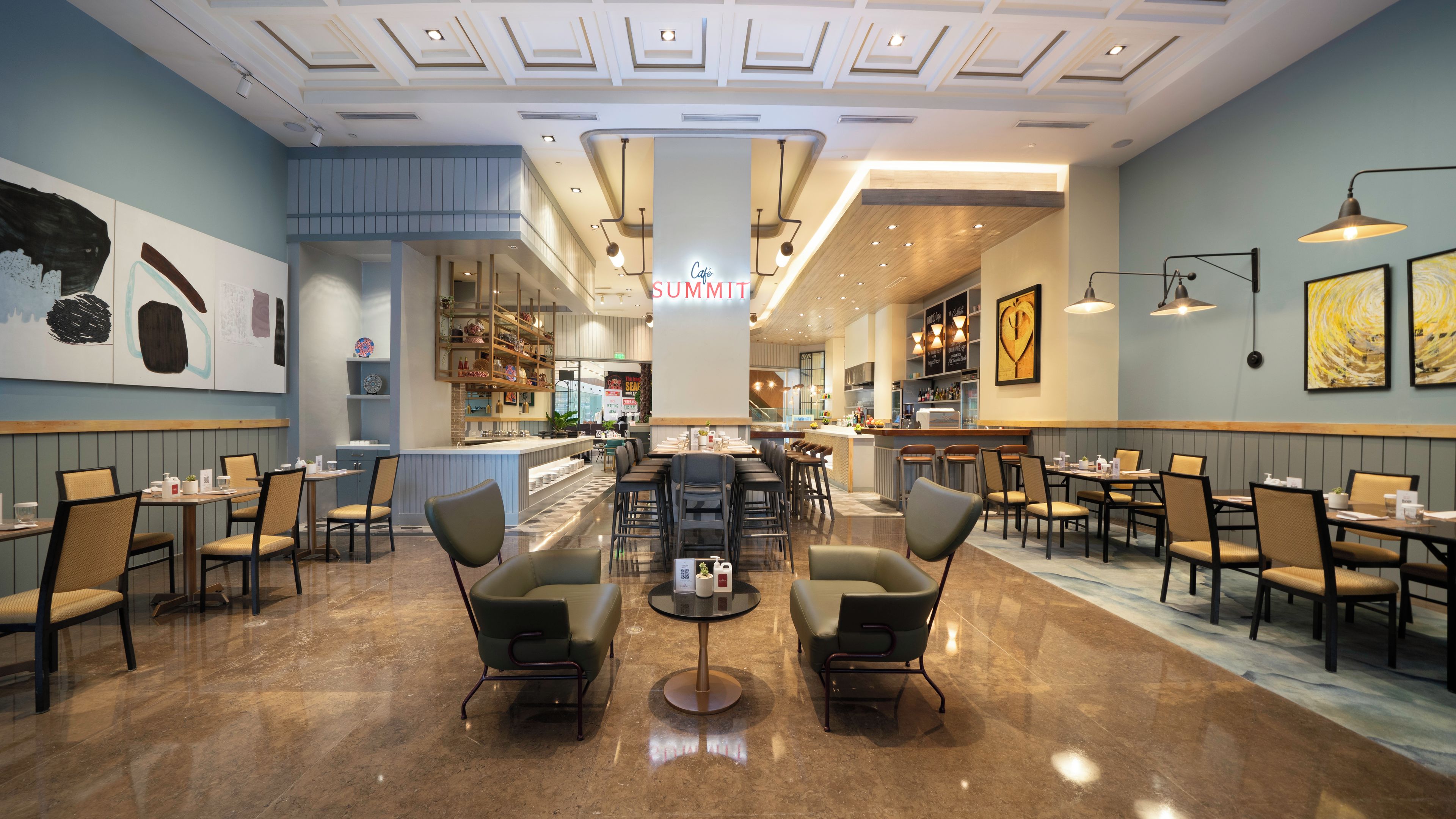 Um hall de hotel moderno com área de bar central, assentos e um letreiro chamativo 'Cafe Summit'.