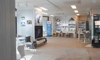 Interior de loja de animais com prateleiras de produtos, uma televisão e camas para animais de estimação.