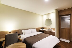 Quarto de hotel com cama, mesa de cabeceira, cadeira e um espelho redondo na parede.