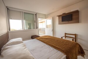 Quarto com cama, cadeira, televisão na parede e janela com persianas.