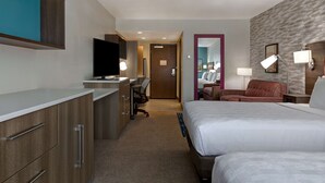 Quarto de hotel com uma cama, escrivaninha, cadeira e televisão.