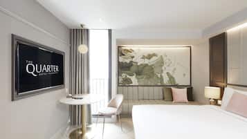 Quarto de hotel moderno com uma cama grande, uma mesa com cadeira, uma televisão na parede e uma grande obra de arte floral sobre a cama.