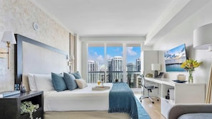 Quarto moderno com cama, escrivaninha e janelas amplas com vista para a cidade.