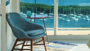 Quarto com vista para um porto e barcos, uma cadeira, um abajur e um tapete.