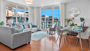 Sala de estar moderna com sofá, mesa de jantar, cadeiras e grandes janelas com vista para a cidade.
