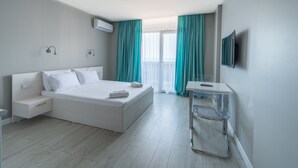Quarto de hotel moderno com uma cama grande, uma mesinha de cabeceira, uma TV presa na parede e uma janela com cortinas.