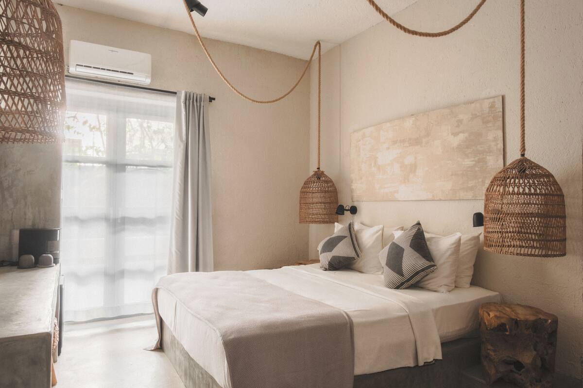 Quarto com cama, mesa de cabeceira e uma janela grande com cortinas.